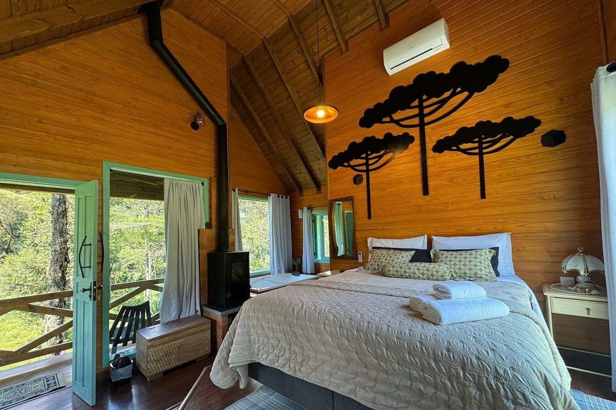 Quarto de cabana de madeira acolhedor, com uma cama grande, lareira e vista para a floresta.