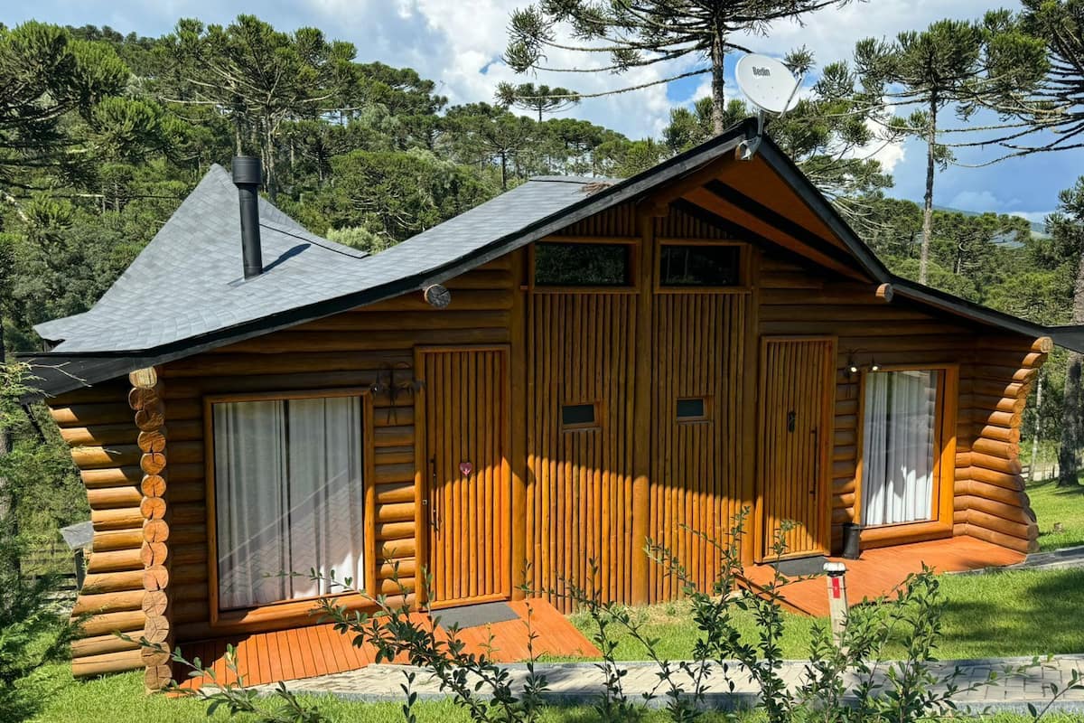 Uma cabana de tronco com telhado inclinado, duas janelas grandes e uma chaminé.