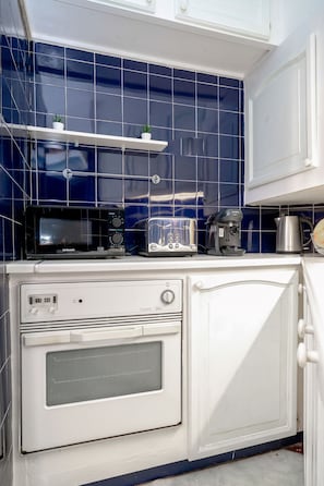 Uma cozinha com forno branco, micro-ondas, torradeira e cafeteira sobre o balcão.