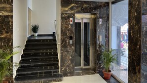 Um hall de hotel moderno com paredes de mármore, escadaria e elevador.