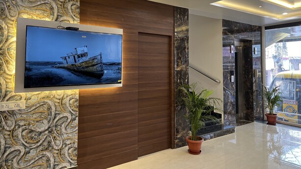 Um hall moderno com uma televisão de tela plana grande presa à parede, um painel de madeira e uma parede de mármore com uma planta em vaso.