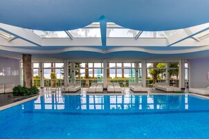 Piscina interna com vista clara para o exterior, incluindo palmeiras e montanhas.