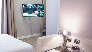 Quarto de hotel com cama, escrivaninha com luminária, televisão e área de jantar com prato, talheres e copo.