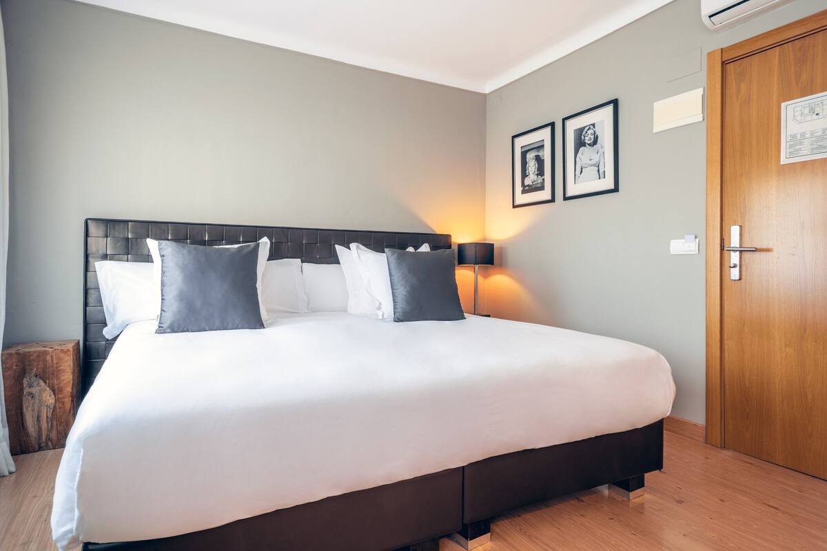 Uma cama bem arrumada com cabeceira, uma luminária de cabeceira e duas molduras na parede.