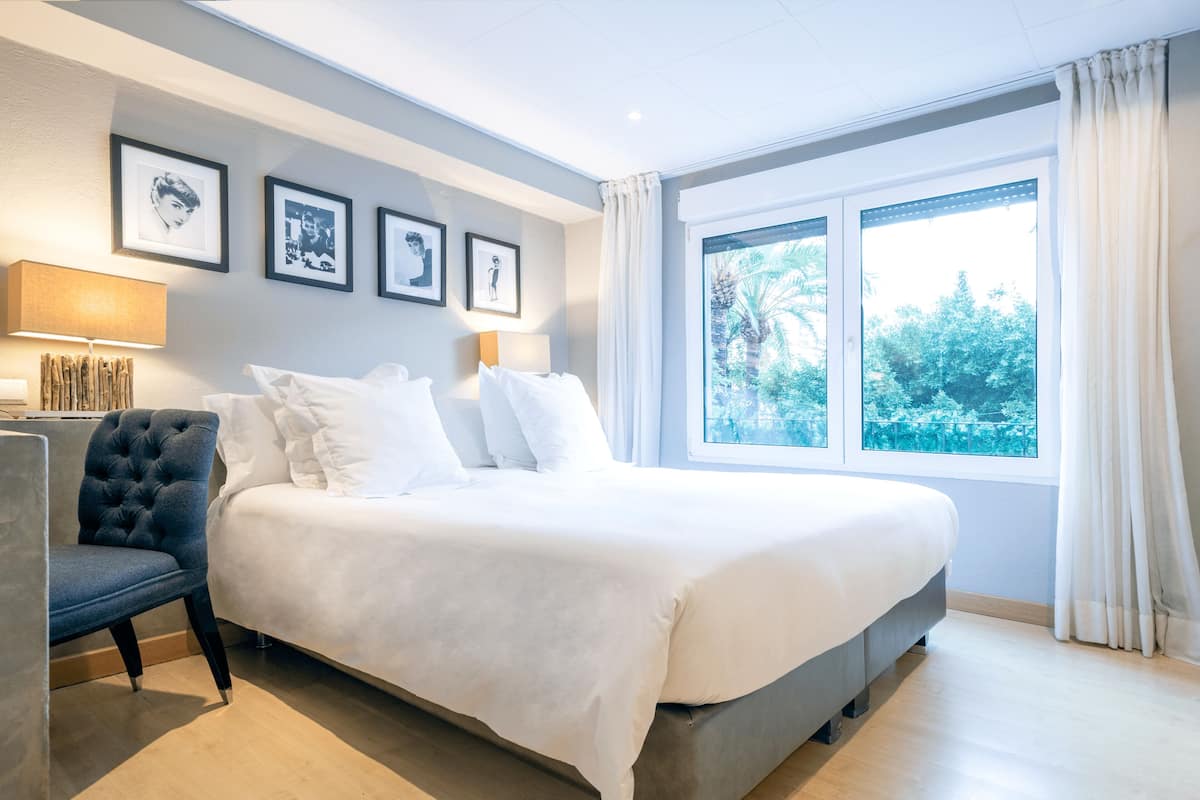 Um quarto bem arrumado com uma cama grande, uma cadeira e quadros nas paredes.