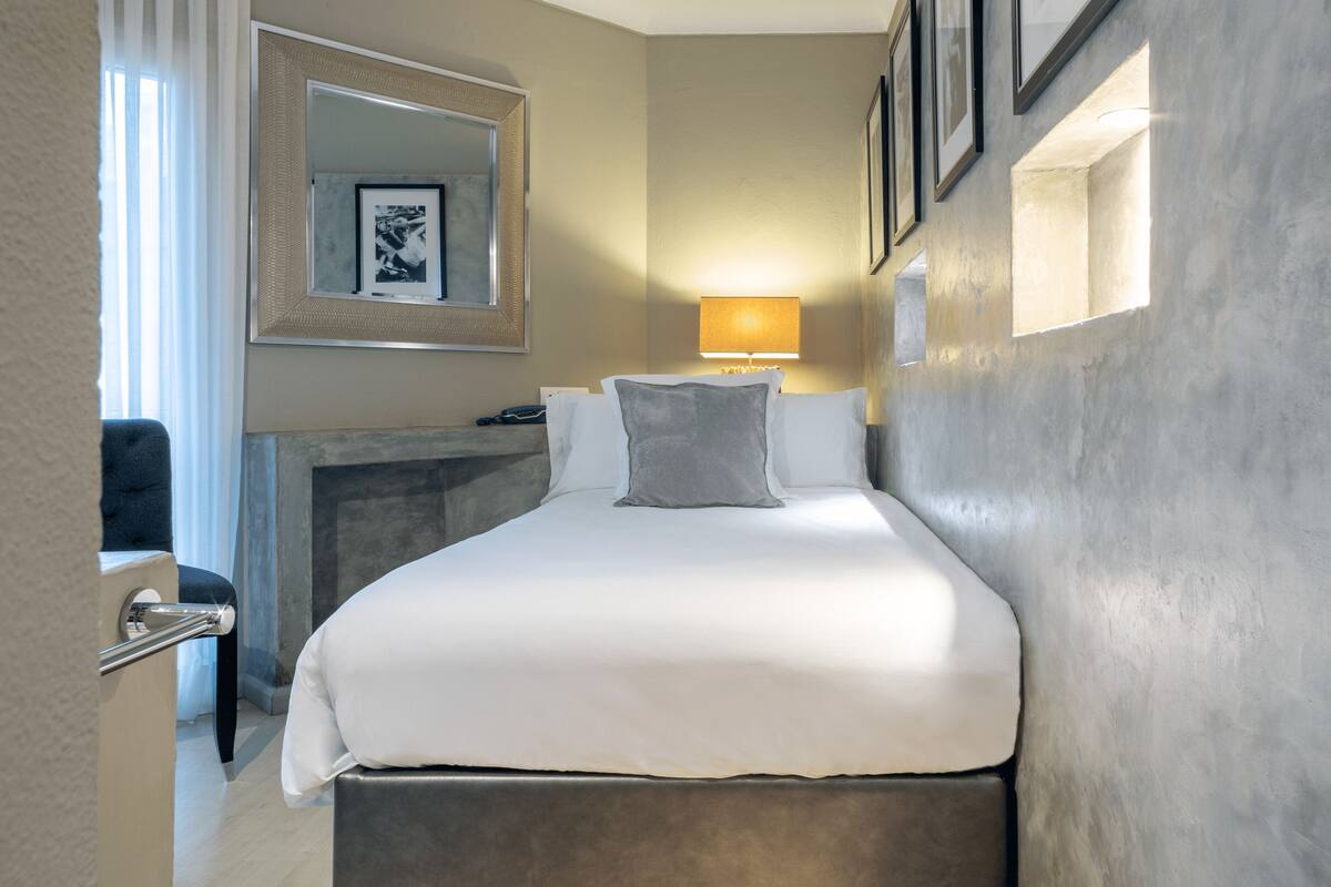 Quarto de hotel com uma cama, mesa de cabeceira, abajur, espelho e um quadro na parede.