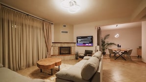 Uma sala de estar com sofá, mesa de centro, lareira, TV e um espaço de jantar com cadeiras e mesa.