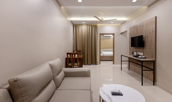 Quarto de hotel moderno com sofá, uma mesinha, televisão e ventoinha no teto.
