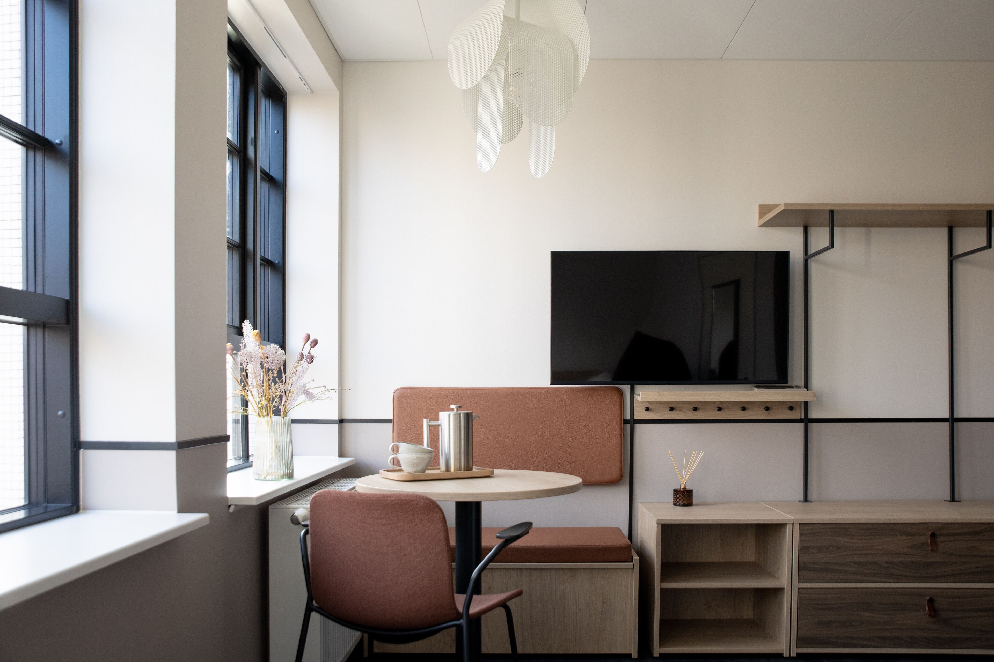 Quarto moderno com uma janela grande, uma mesa redonda com uma cadeira, uma televisão e um armário de madeira.