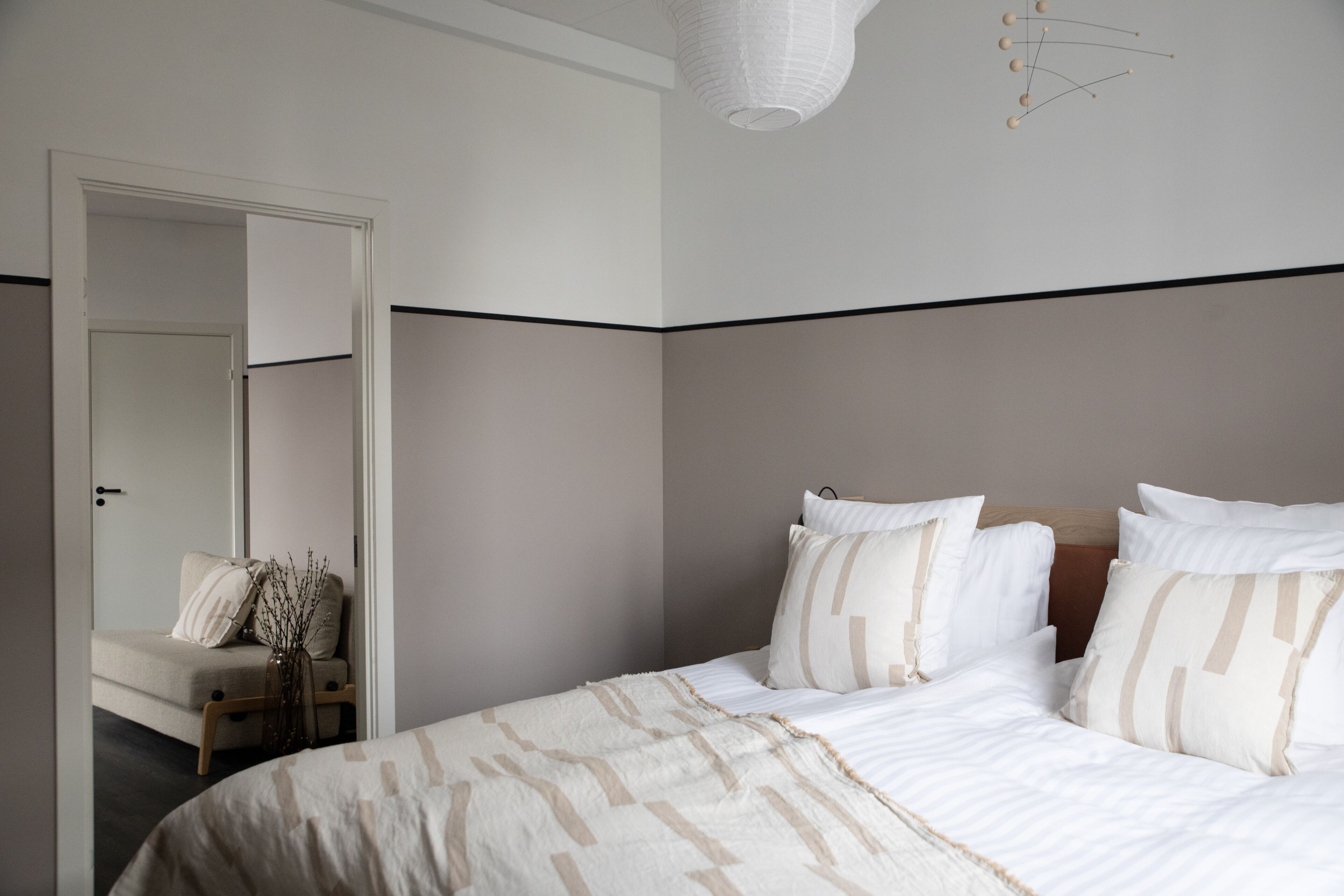 Quarto com cama, uma cadeira e porta que dá para outro cômodo.
