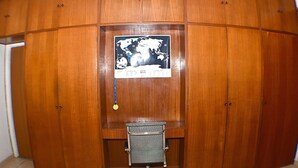Um guarda-roupa de madeira com um cartaz de mapa-múndi, uma cadeira de escritório pequena e um tapete vermelho.