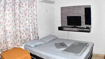 Quarto com cama, televisão na parede, mesa pequena e cortina com padrão floral.