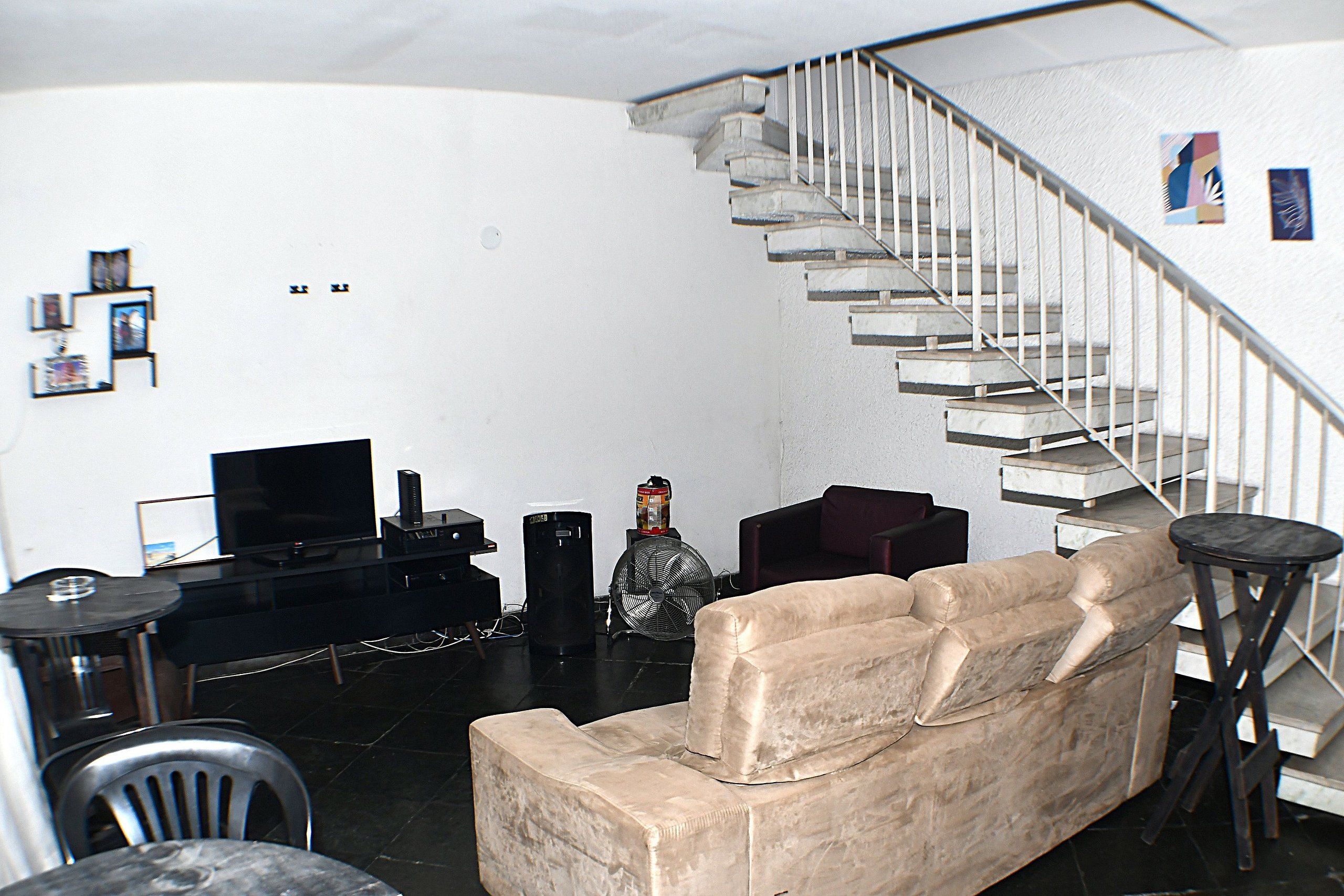 Uma sala de estar com sofá, televisão, ventilador e escada.