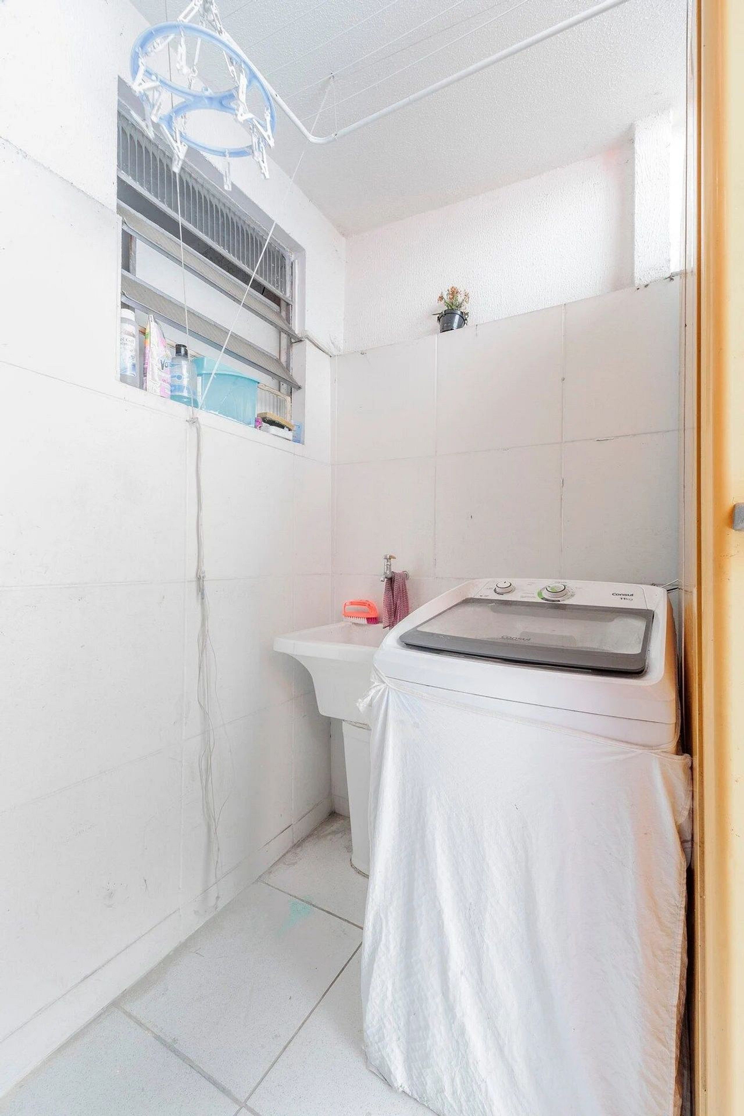 Um banheiro pequeno revestido com azulejos, com máquina de lavar, janela e pia.