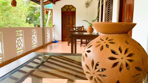 Área externa coberta com piso de azulejos, um vaso de terracota grande e uma porta de madeira.