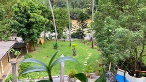 Um jardim exuberante com diversas plantas e árvores, um pequeno gramado e um caminho que leva a um edifício.