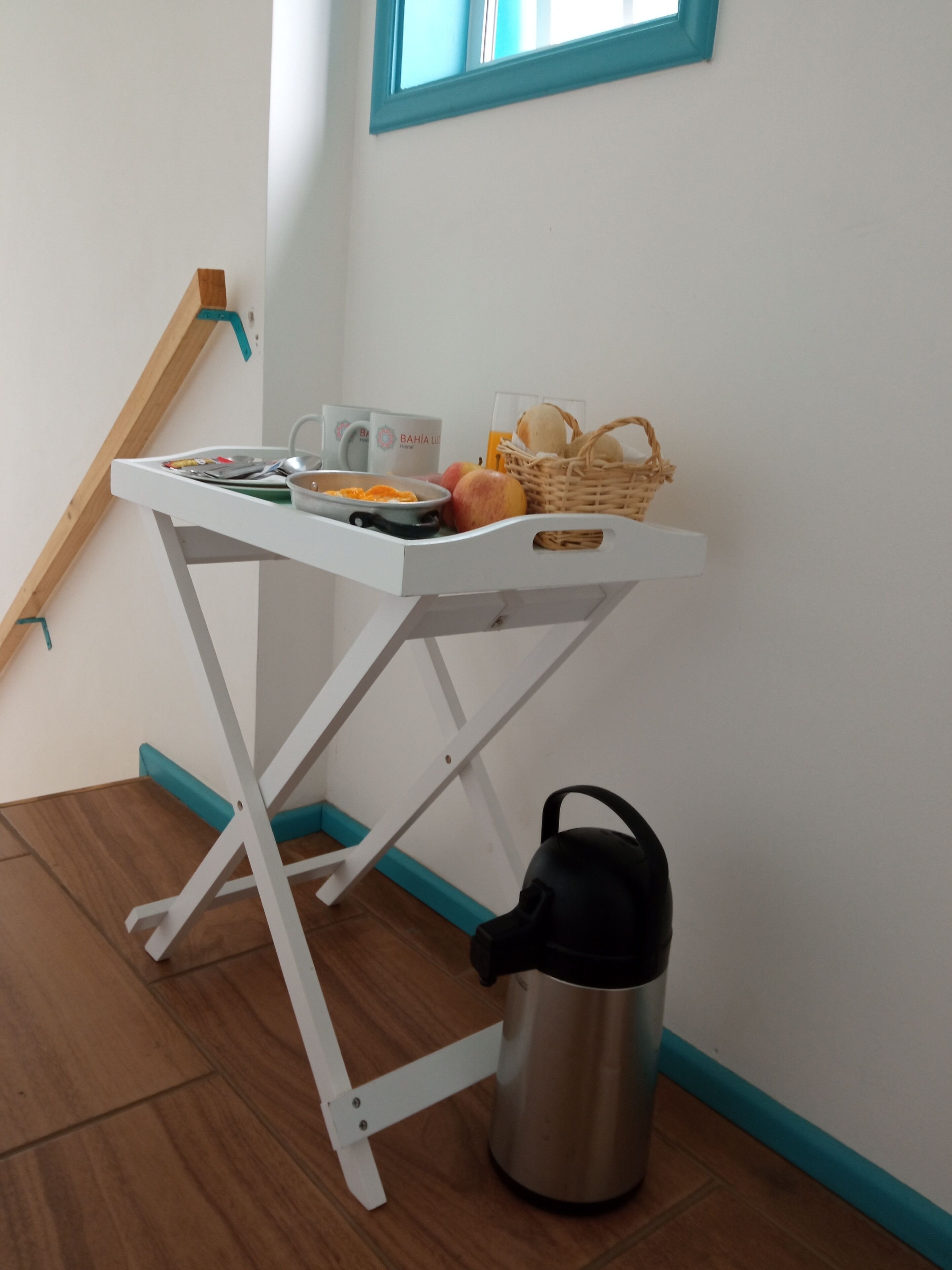 Uma mesa branca com uma chaleira, um cesto e itens de pequeno-almoço.