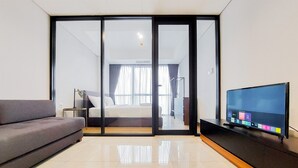 Quarto de hotel moderno com sofá, televisão de tela plana, cama e porta de vidro deslizante para uma varanda.