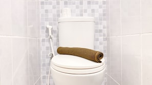 Sanitário com caixa de descarga e assento brancos, rolo de papel higiênico marrom e suporte branco para papel.