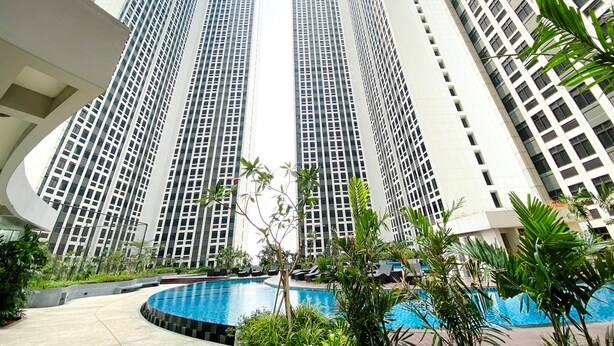 Um edifício moderno de vários andares com piscina, rodeado por vegetação.