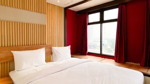 Quarto de hotel moderno com uma cama grande, cabeceira de madeira e vista para a cidade através de grandes janelas.