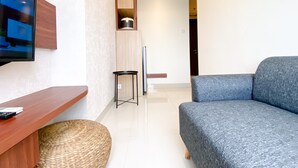 Uma sala de estar moderna com uma TV de tela plana, uma estante de madeira, um banquinho tecido, um sofá azul e um pequeno banquinho preto.