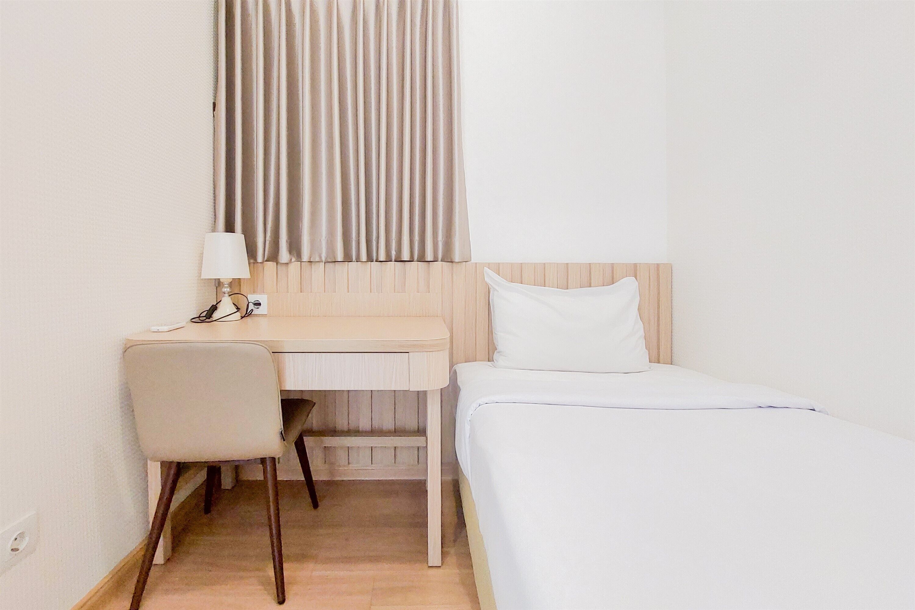 Quarto de hotel pequeno e bem organizado, com uma cama, uma escrivaninha e uma cadeira.