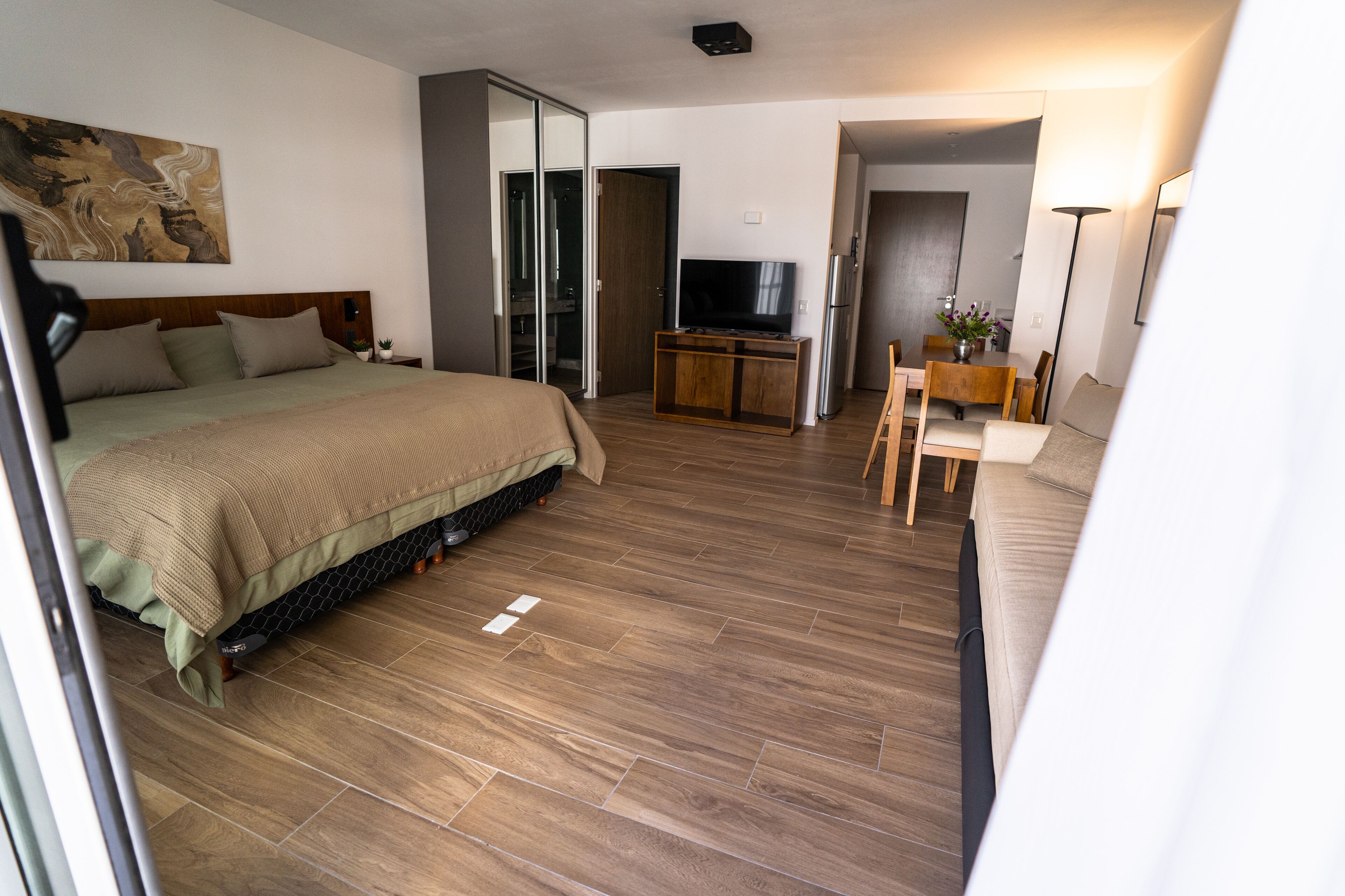 Quarto de hotel moderno com uma cama grande, televisão, área de jantar e closet espaçoso.