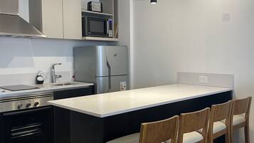 Cozinha moderna com ilha central, eletrodomésticos embutidos e banquetas de madeira.