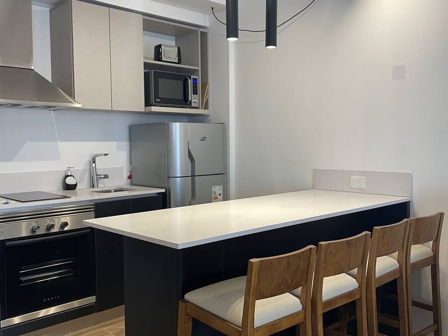 Cozinha moderna com ilha central, eletrodomésticos embutidos e banquetas de madeira.