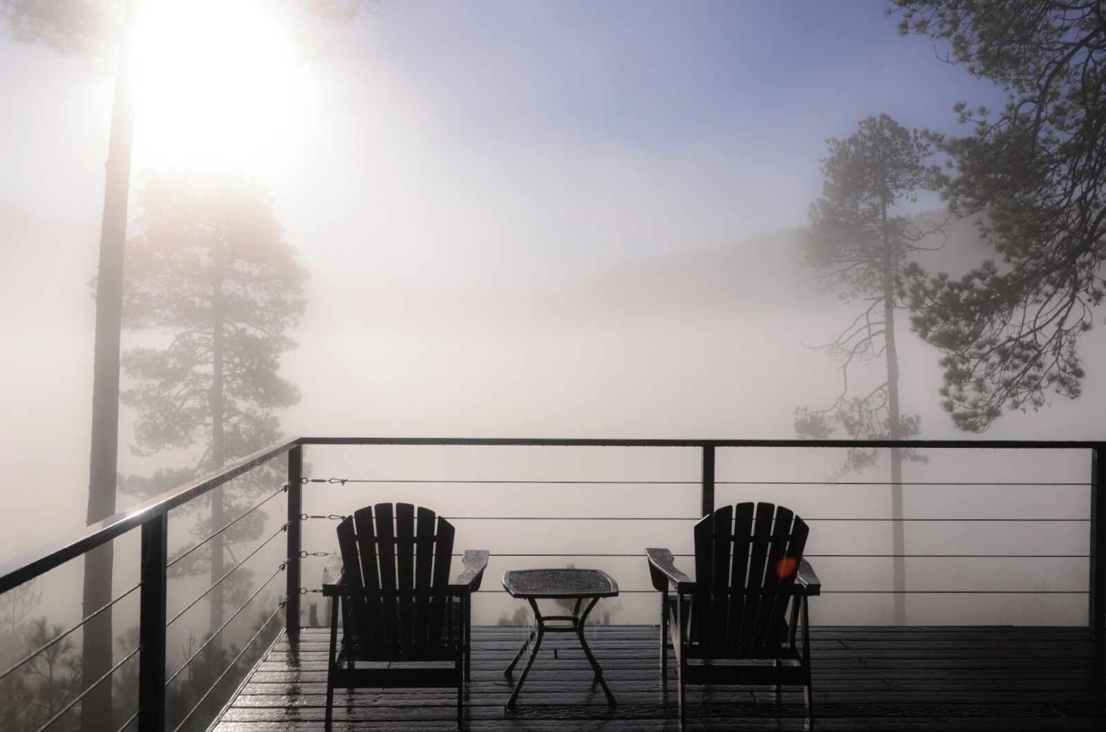 Um terraço ao ar livre com névoa, duas cadeiras Adirondack e uma pequena mesa.