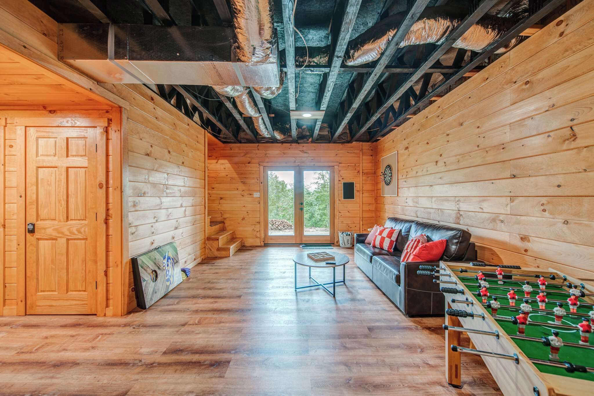 Um quarto acolhedor com paredes de madeira, um sofá, uma mesa de futebol e uma porta que dá para uma área externa.