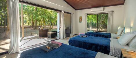 Quarto com duas camas, uma janela grande e vista para árvores.