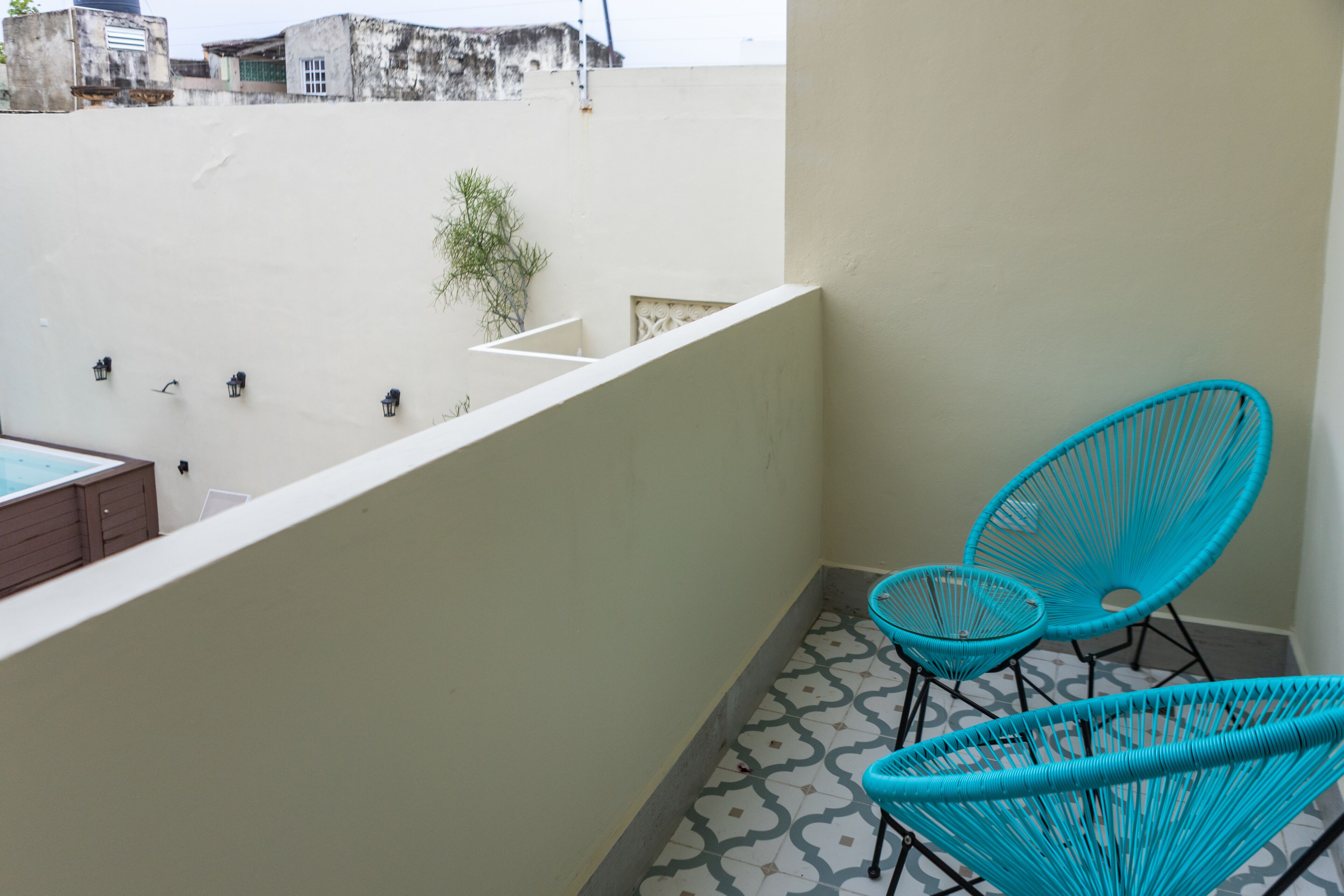 Uma varanda com duas cadeiras turquesa, uma mesa pequena e vista para prédios ao longe.