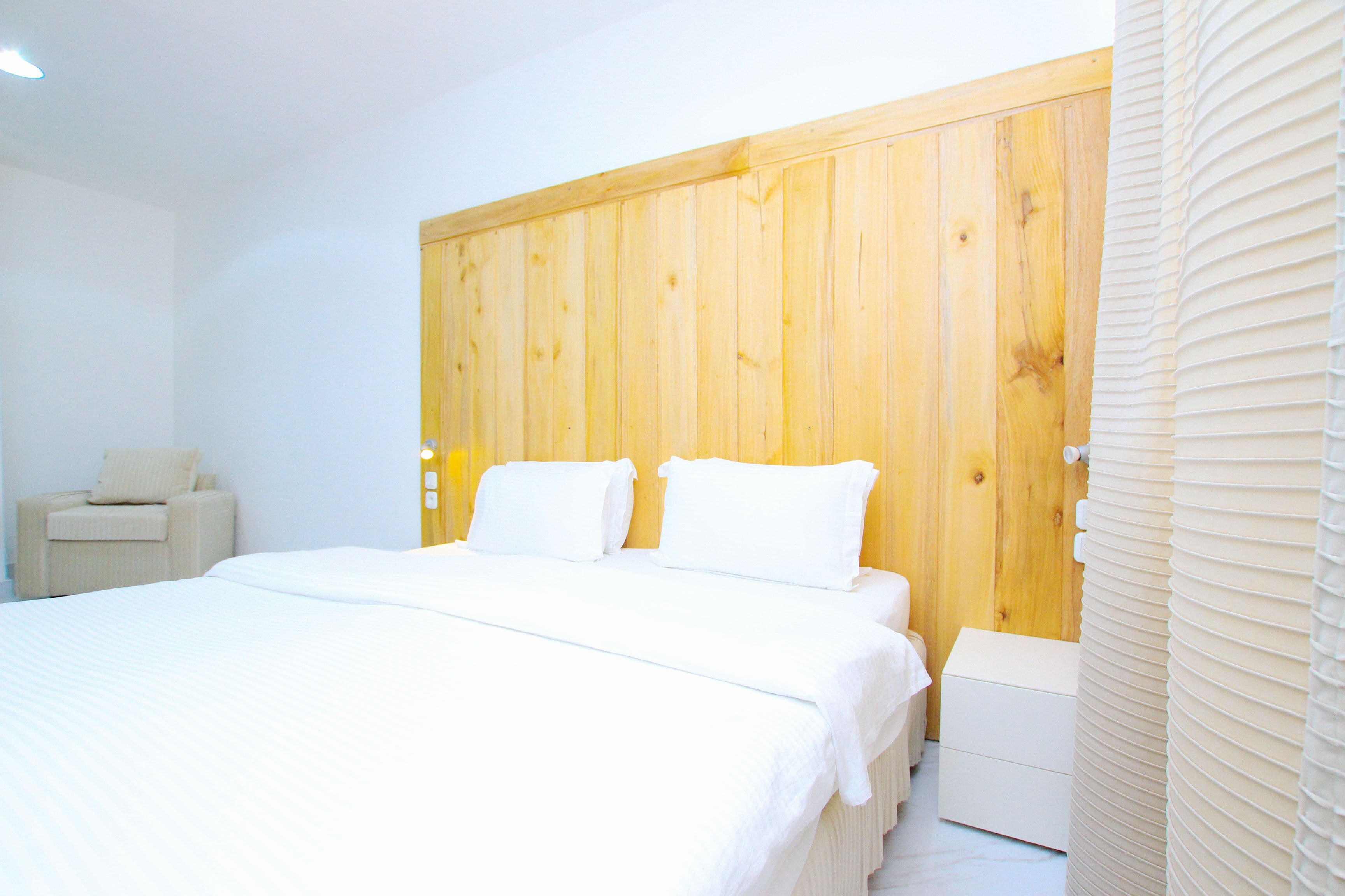 Quarto com cabeceira de madeira, cama com roupa de cama branca, mesa de cabeceira e criado-mudo.