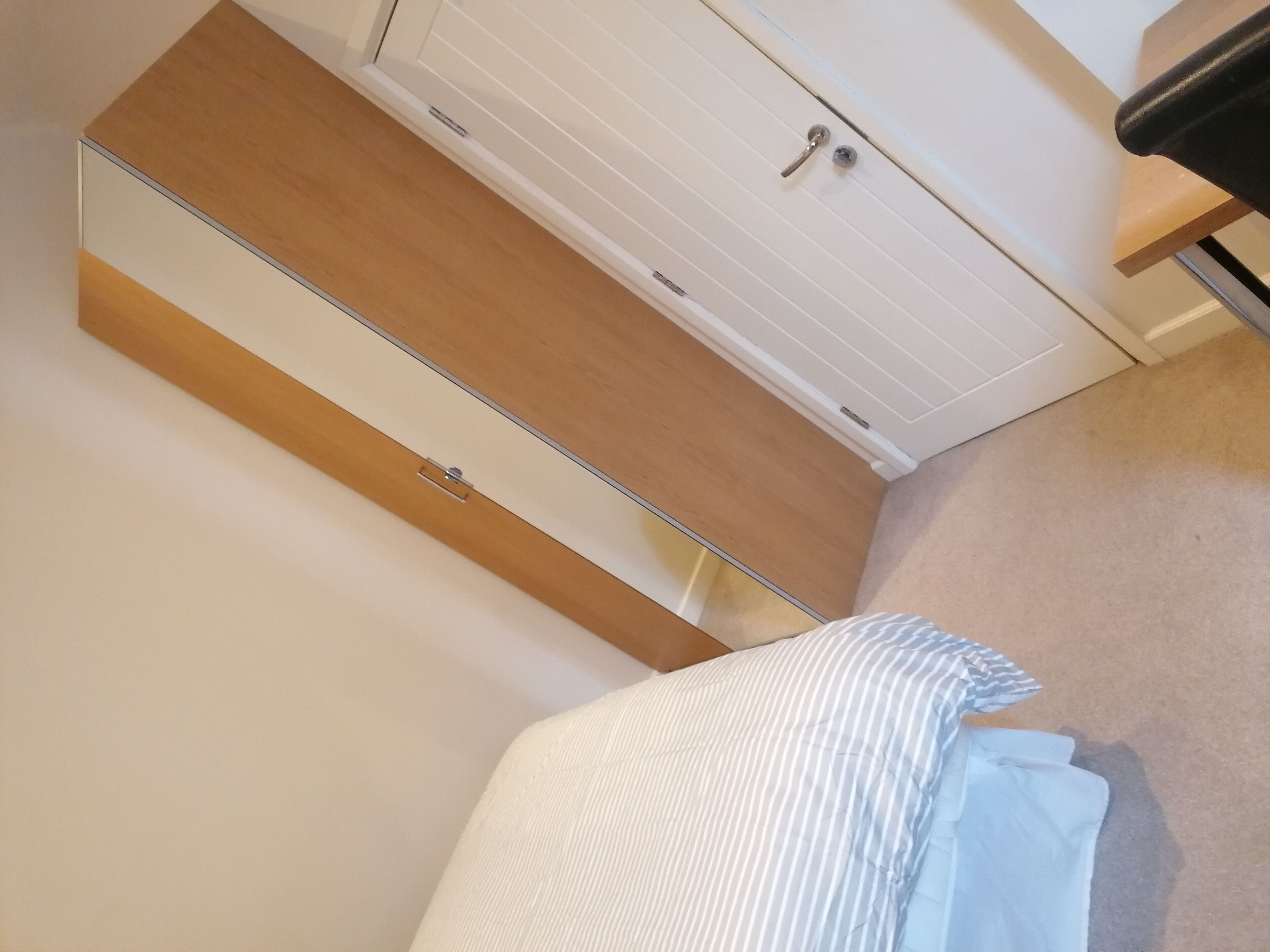 Quarto com piso de madeira, guarda-roupa branco e cama com travesseiro listrado.