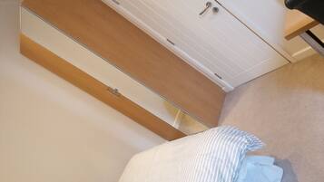 Quarto com piso de madeira, guarda-roupa branco e cama com travesseiro listrado.