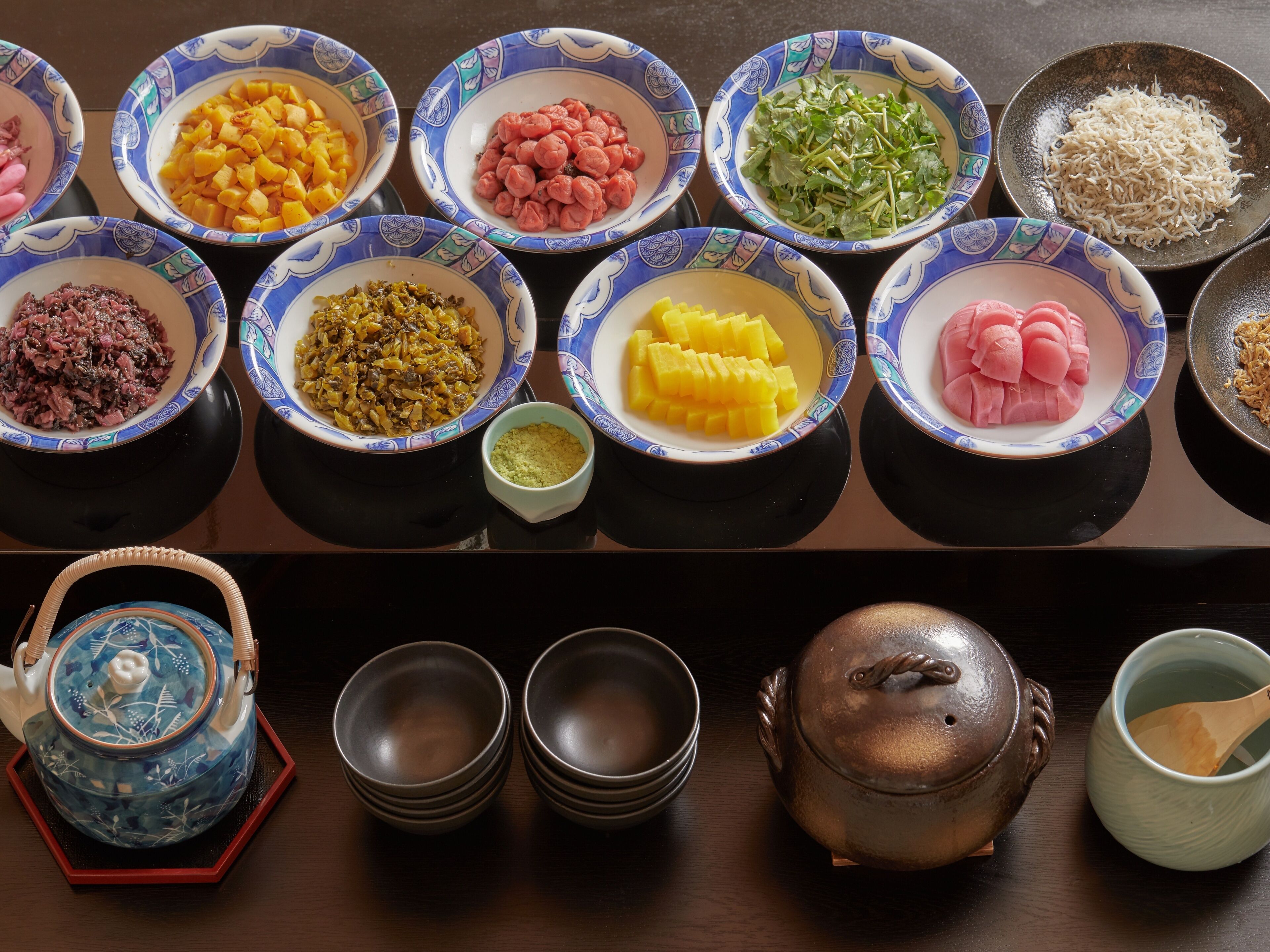 Diversos pratos em tigelas sobre uma mesa, um bule e várias xícaras.