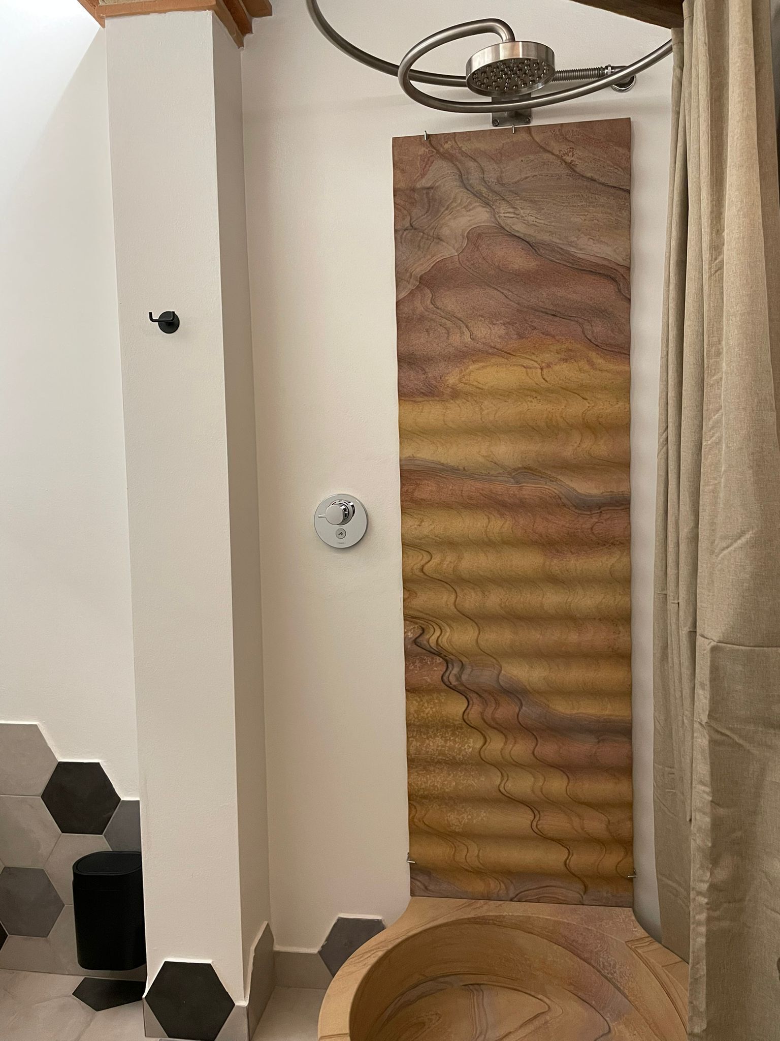 Um chuveiro com parede de mármore, um chuveiro no teto e um padrão de azulejos hexagonais no chão.