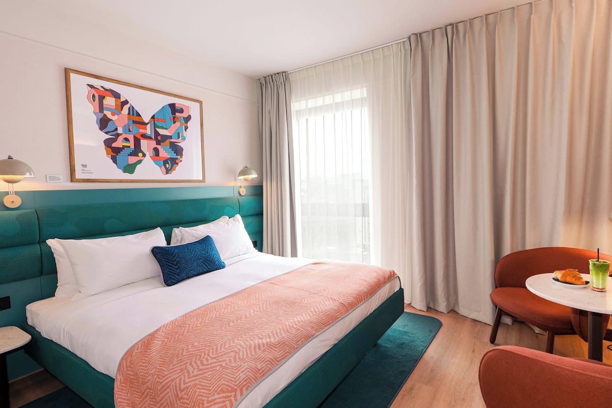 Quarto de hotel com cama, cadeira, mesa e janela com cortinas.