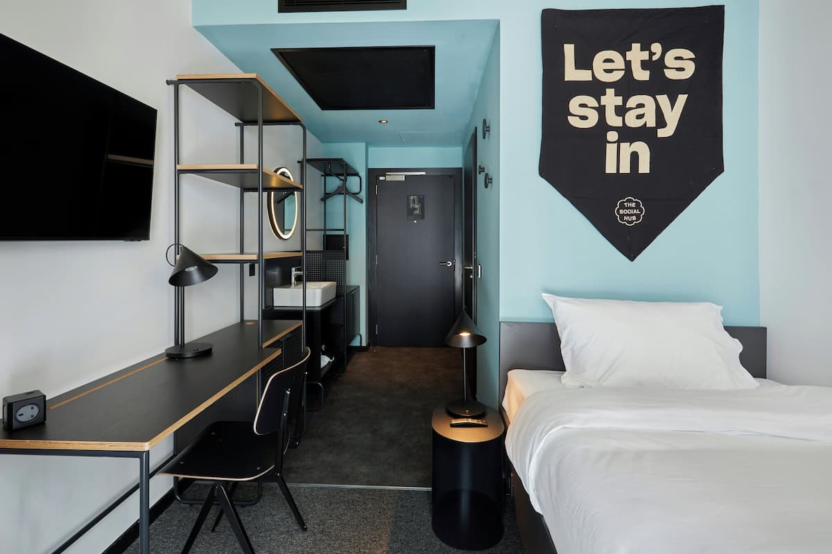 Quarto de hotel moderno com escrivaninha, cadeira, cama e um sinal fixado na parede.