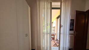 Quarto com chão de azulejos, porta de madeira e vista para um pátio externo com cadeiras e uma mesa.