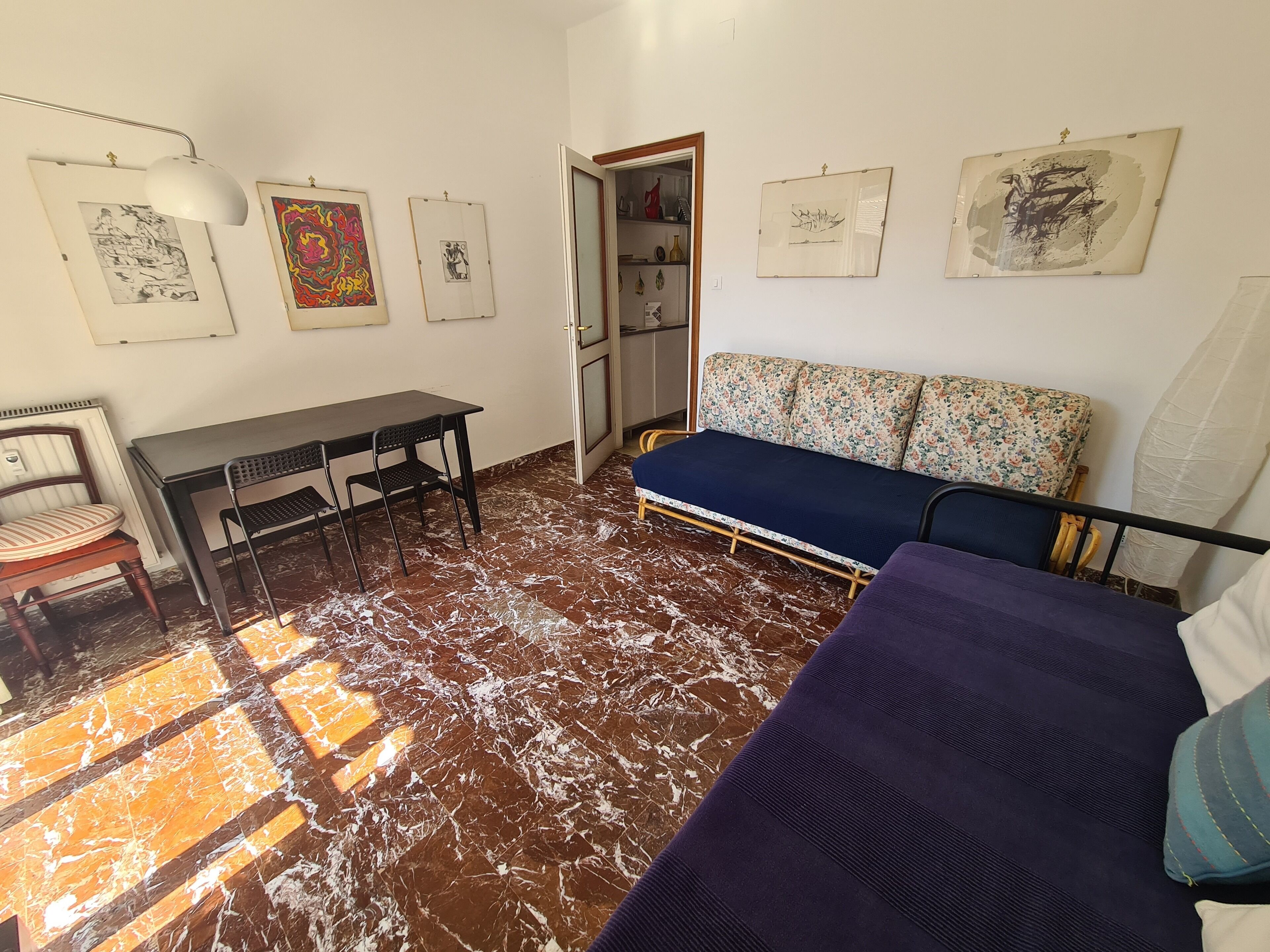 Quarto com cama, escrivaninha, cadeira e sofá. Há quadros nas paredes e um radiador.
