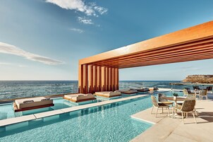 Piscina infinita no terraço com espreguiçadeiras e pérgola de madeira, com vista para o mar.