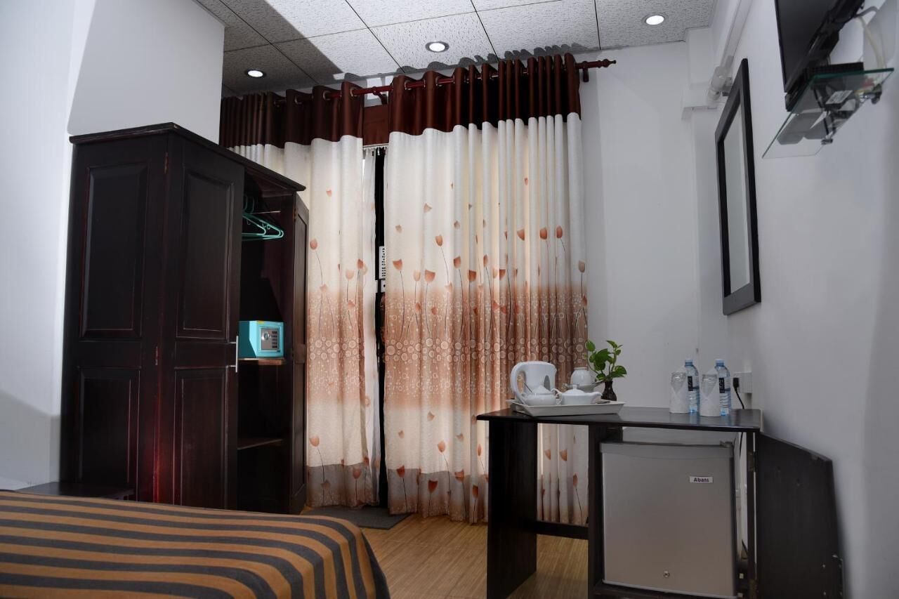 Quarto de hotel com cama, escrivaninha com chaleira, pequeno armário e guarda-roupa.