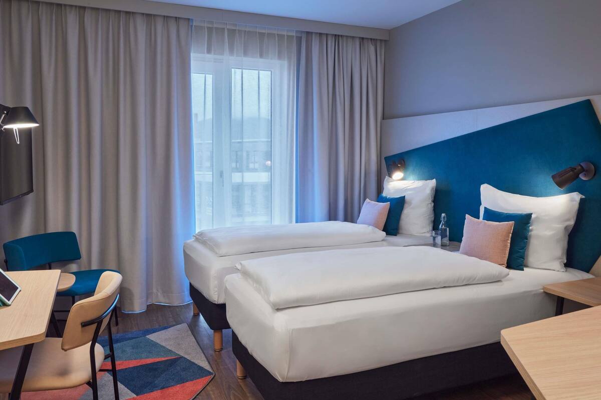 Quarto de hotel com uma cama grande, duas mesas de cabeceira, uma escrivaninha e uma cadeira.