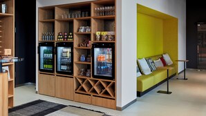 Uma área comercial com prateleiras cheias de diversos produtos, um espaço de descanso com almofadas e um refrigerador com bebidas.
