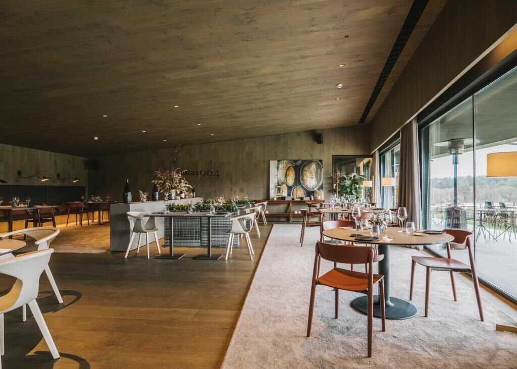 Um restaurante espaçoso com decoração moderna, destacando um balcão central, diversas opções de assentos e amplas janelas com vista para o exterior.