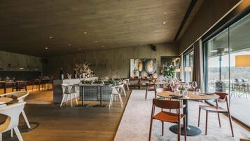 Um restaurante espaçoso com decoração moderna, destacando um balcão central, diversas opções de assentos e amplas janelas com vista para o exterior.