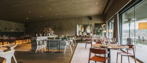 Um restaurante espaçoso com decoração moderna, destacando um balcão central, diversas opções de assentos e amplas janelas com vista para o exterior.